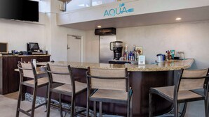 Uma área de bar com balcão, banquetas, uma máquina de café e uma TV fixada na parede.