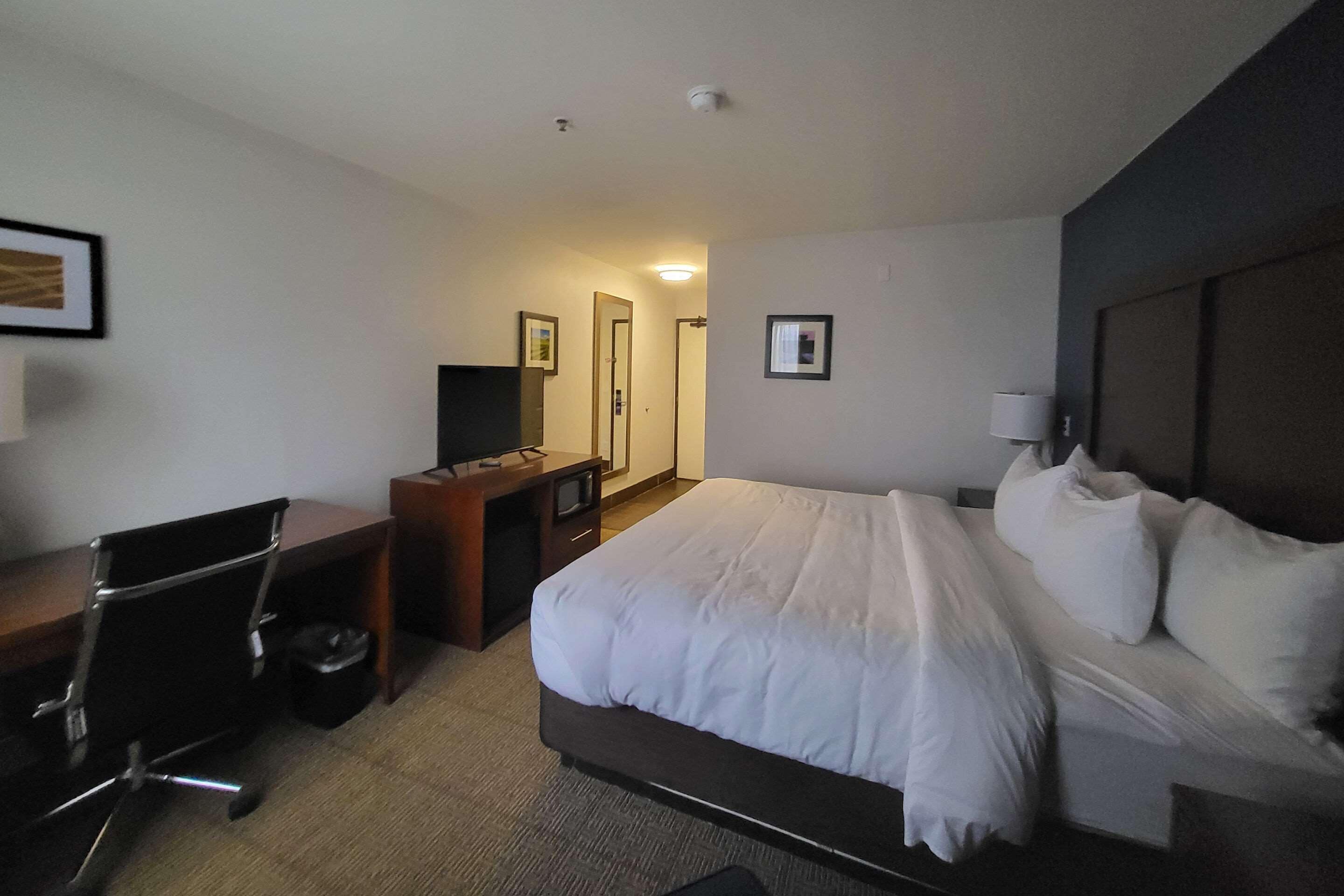 Quarto de hotel com cama, escrivaninha, cadeira, televisão e uma pequena mesa.