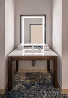 Casa de banho com lavatório branco, toucador de madeira e um espelho grande.