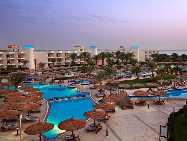 Resort com várias piscinas, áreas de descanso com guarda-sóis e vista para o mar.