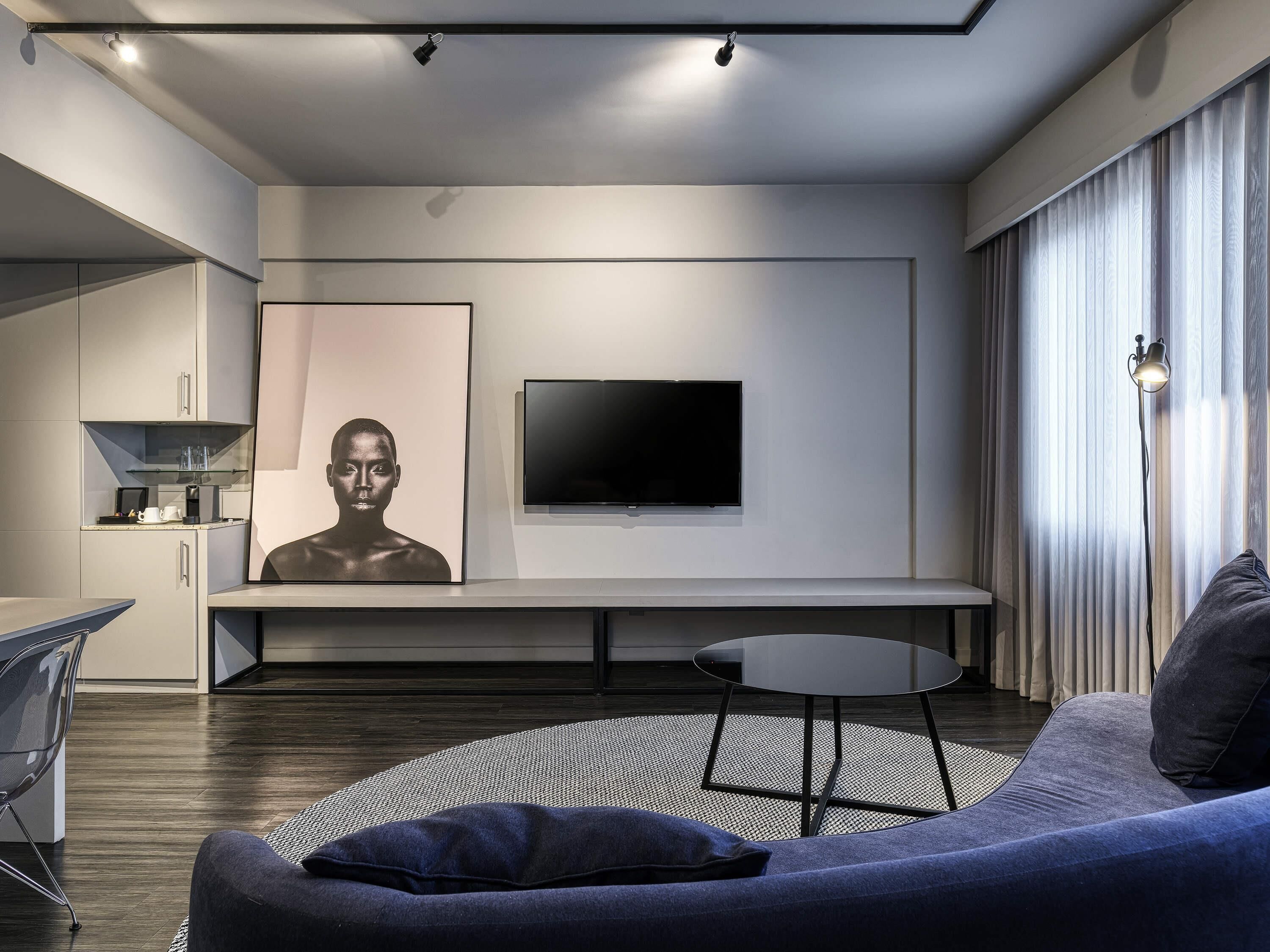 Uma sala de estar moderna com televisão de tela plana, uma grande obra de arte emoldurada, um sofá e uma pequena mesa redonda.