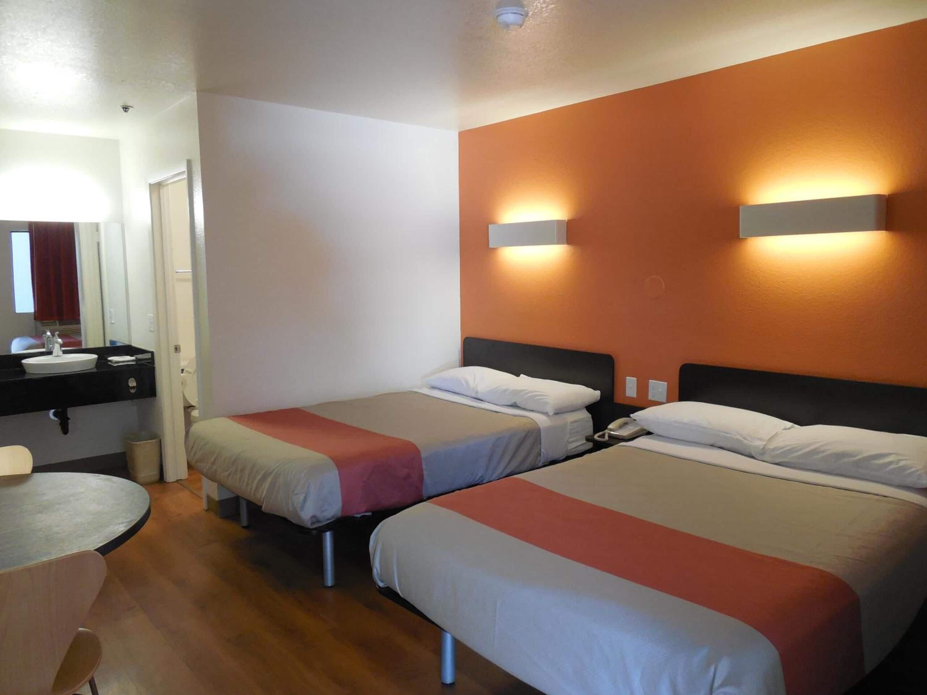 Quarto de hotel com duas camas, uma secretária pequena e casa de banho.