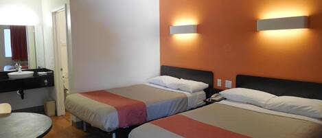 Quarto de hotel com duas camas, uma secretária pequena e casa de banho.