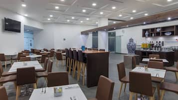 Uma sala de jantar moderna com várias mesas e cadeiras, um buffet e um relógio na parede.