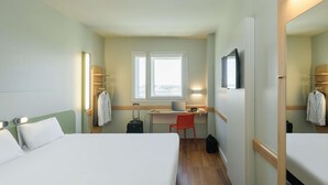 Quarto de hotel com duas camas, uma mesa, uma cadeira, uma mala e uma televisão.