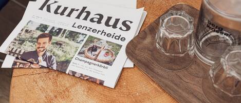 Um jornal com o título 'Kurhaus Lenzerheide' e uma fotografia de um homem e uma cesta de champanhe.