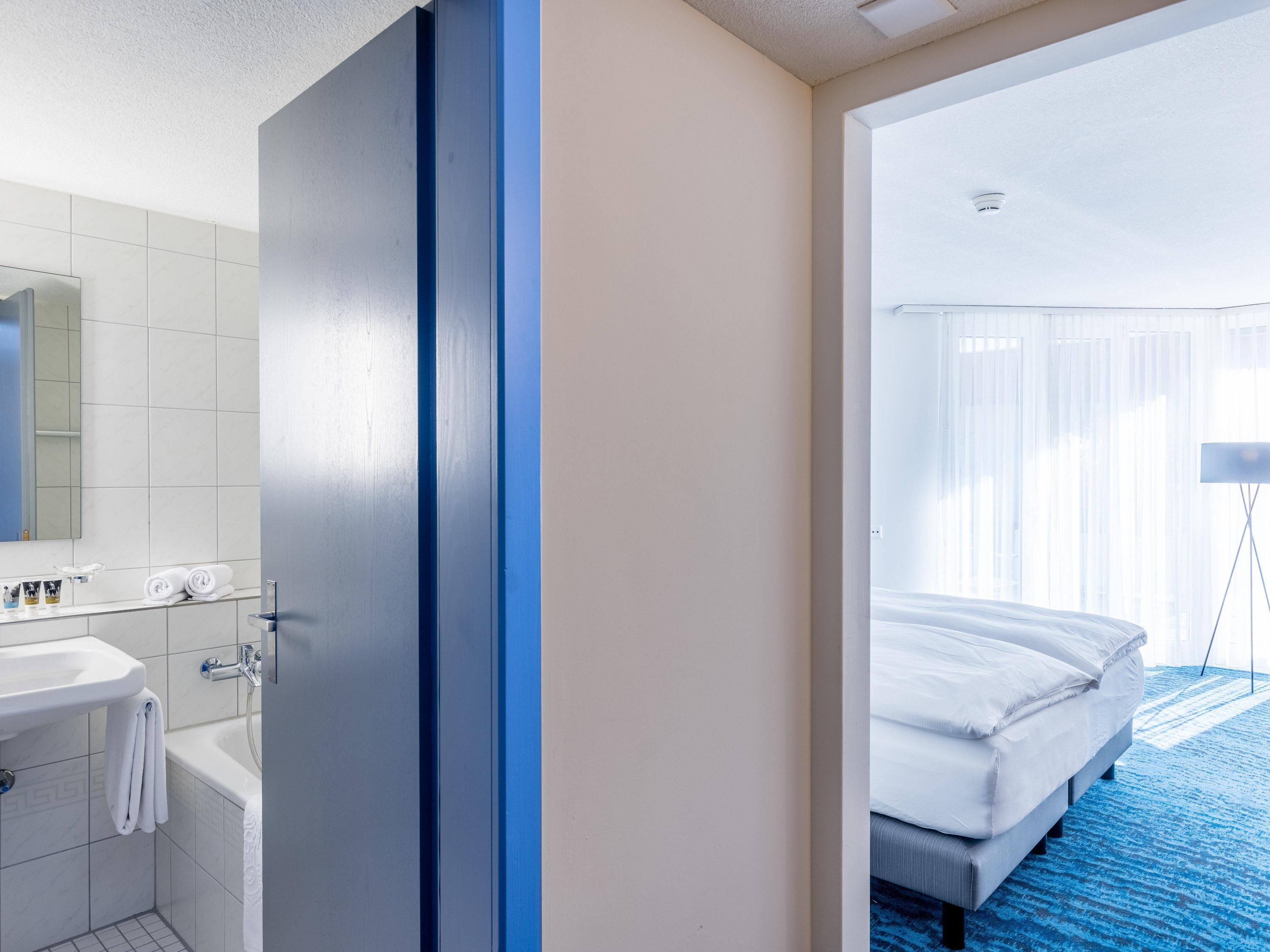 Quarto de hotel com banheiro, cama e uma janela grande.