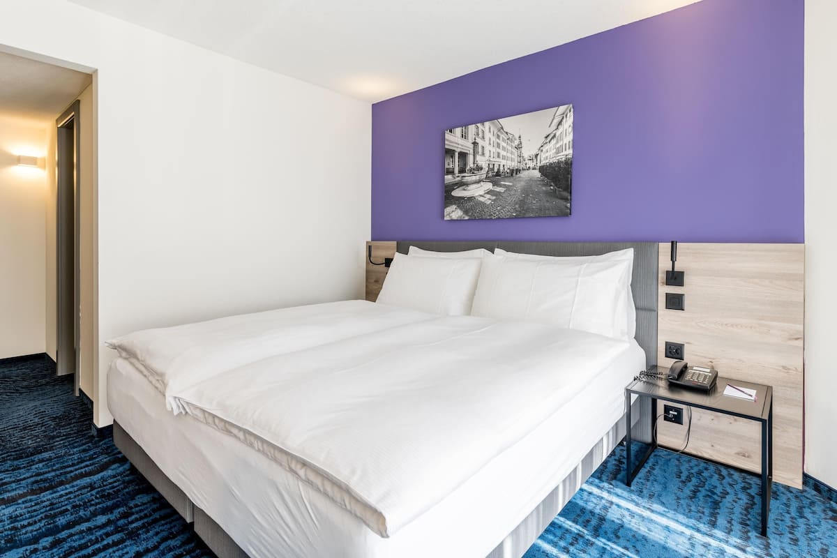 Quarto de hotel com uma cama, uma mesa de cabeceira com telefone e um quadro na parede.