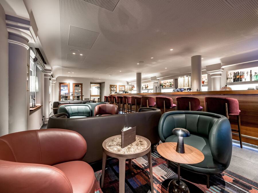 Um hall de hotel moderno com assentos de couro, área de bar e carpete estampado.