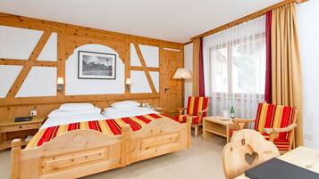 Quarto de hotel com uma cama grande, duas cadeiras, uma mesinha e uma escrivaninha.