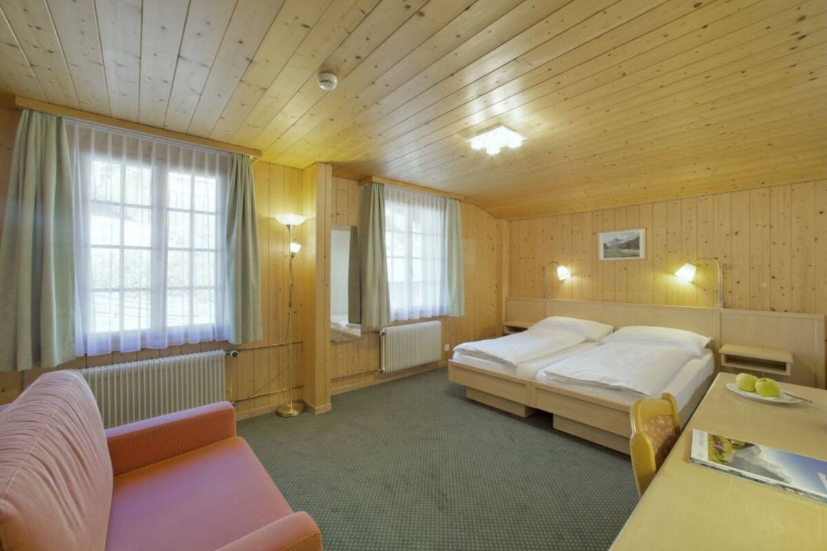 Quarto com painéis de madeira, uma cama de casal, um sofá, uma mesa com um prato de maçãs e um radiador.