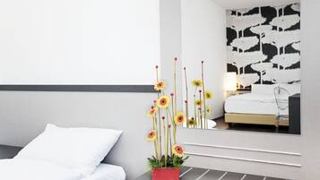 Quarto de hotel moderno com uma cama, uma mesa de cabeceira com um vaso de flores vermelho, um espelho refletindo o quarto e uma parede com padrão preto e branco.