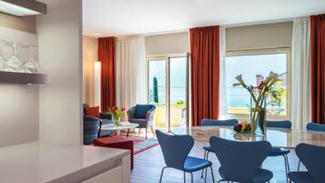 Quarto de hotel moderno com varanda, área de refeições com cadeiras azuis e uma mesa com um vaso de flores.