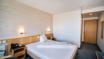 Quarto de hotel com cama, mesas de cabeceira, escrivaninha e uma cadeira.