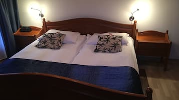 Cama bem arrumada com almofadas florais, duas mesas de cabeceira com abajures e um cabeceiro de madeira.
