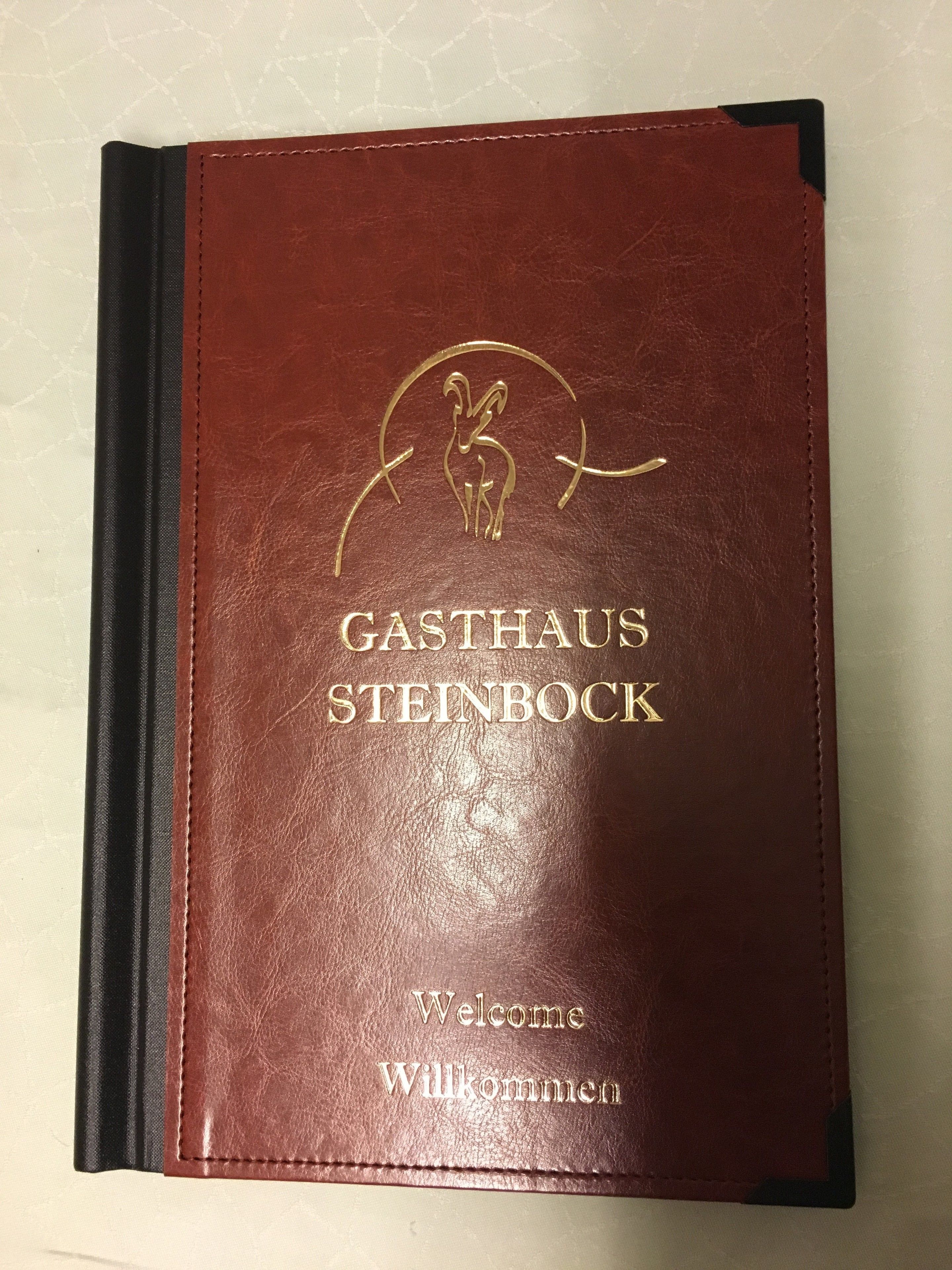 Um livro encadernado em couro marrom, com texto em relevo e um logotipo, intitulado "GASTHAUS STEINBOCK".
