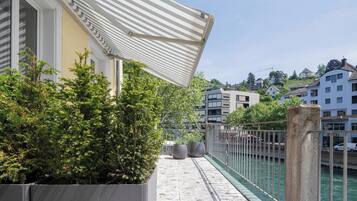 Uma varanda com vista para um rio, cercada por vegetação e edifícios modernos.