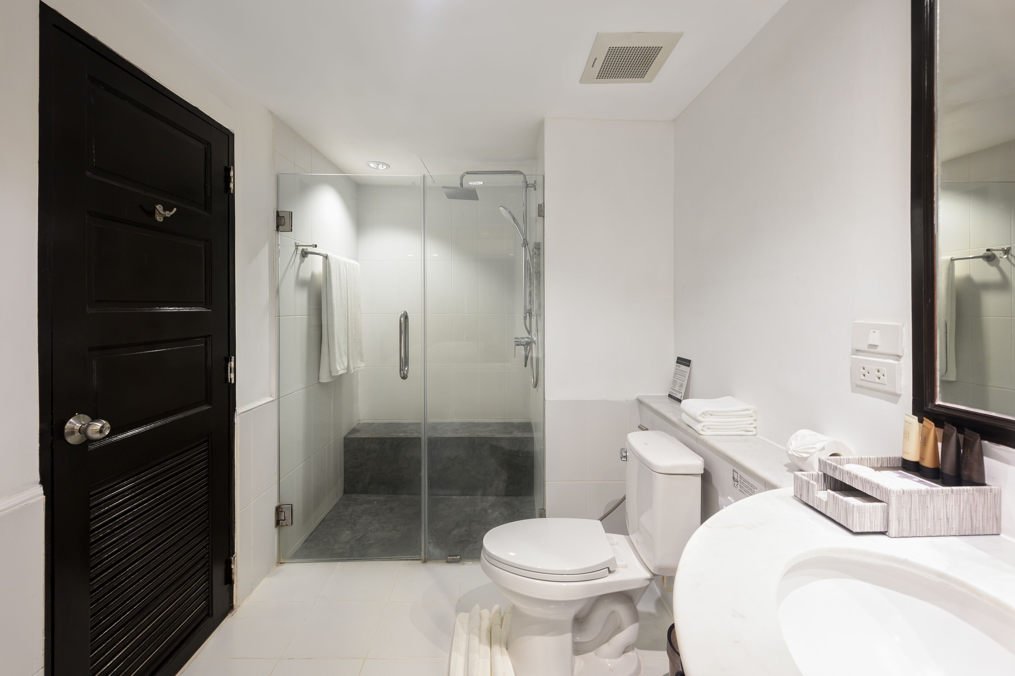 Uma casa de banho moderna com cabine de duche em vidro, sanita branca e toucador com espelho.
