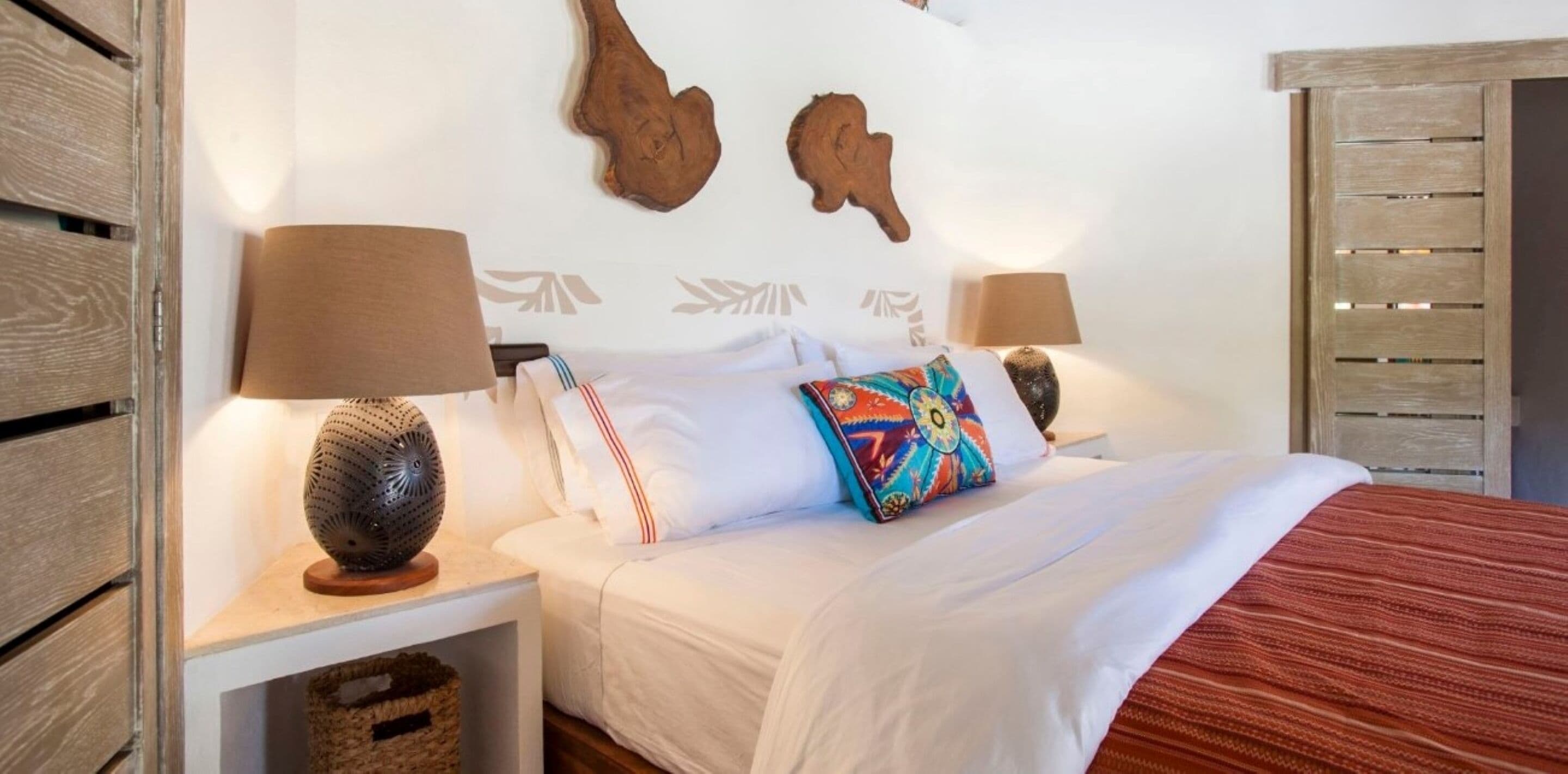Cama bem arrumada com lençóis brancos, duas luminárias de cabeceira e uma almofada decorativa colorida.