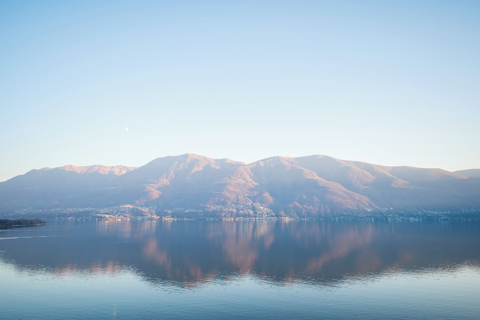 Uma cordilheira refletida num lago calmo, com uma cidade ao primeiro plano.