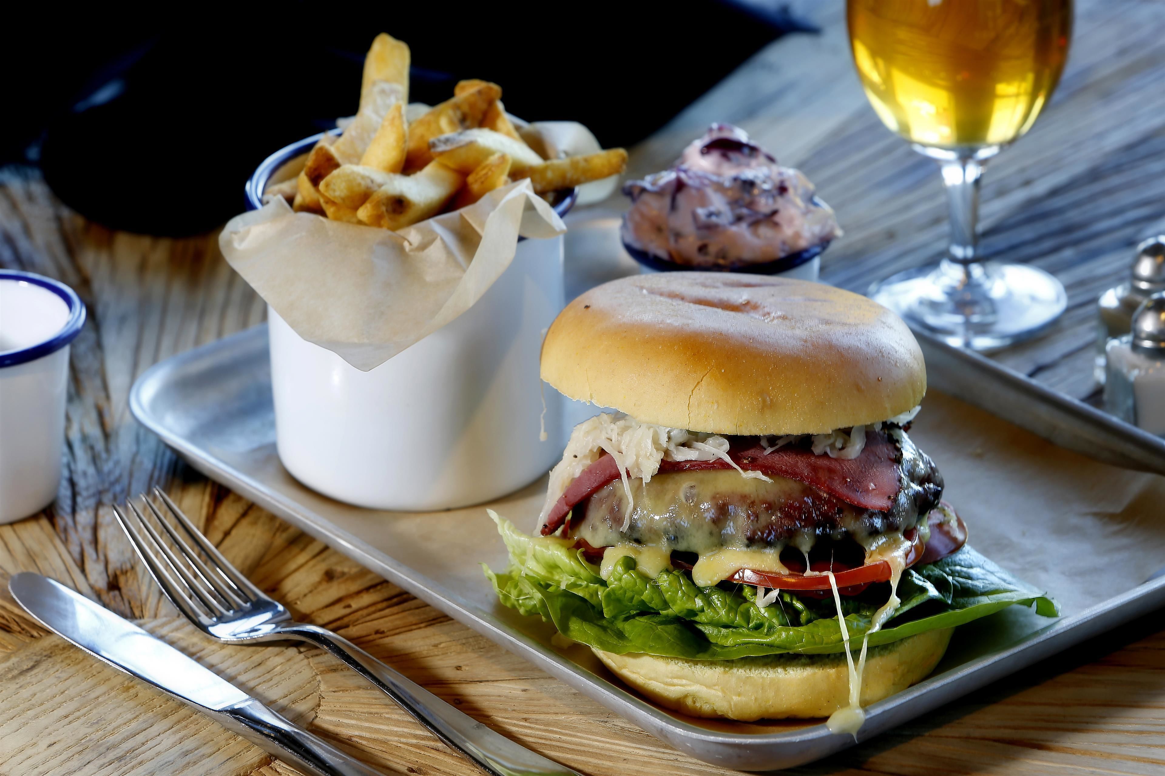 Uma refeição com hambúrguer, batatas fritas e um copo de cerveja sobre uma mesa de madeira.