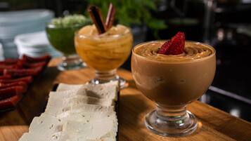 Uma tábua de madeira com diversos alimentos, incluindo uma sobremesa de chocolate, uma tigela verde e uma seleção de queijos.
