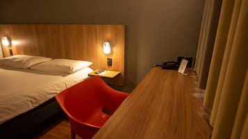 Quarto de hotel com cabeceira de madeira, cama com roupa de cama branca, uma cadeira vermelha e uma mesa de madeira com um telefone e um bloco de notas.