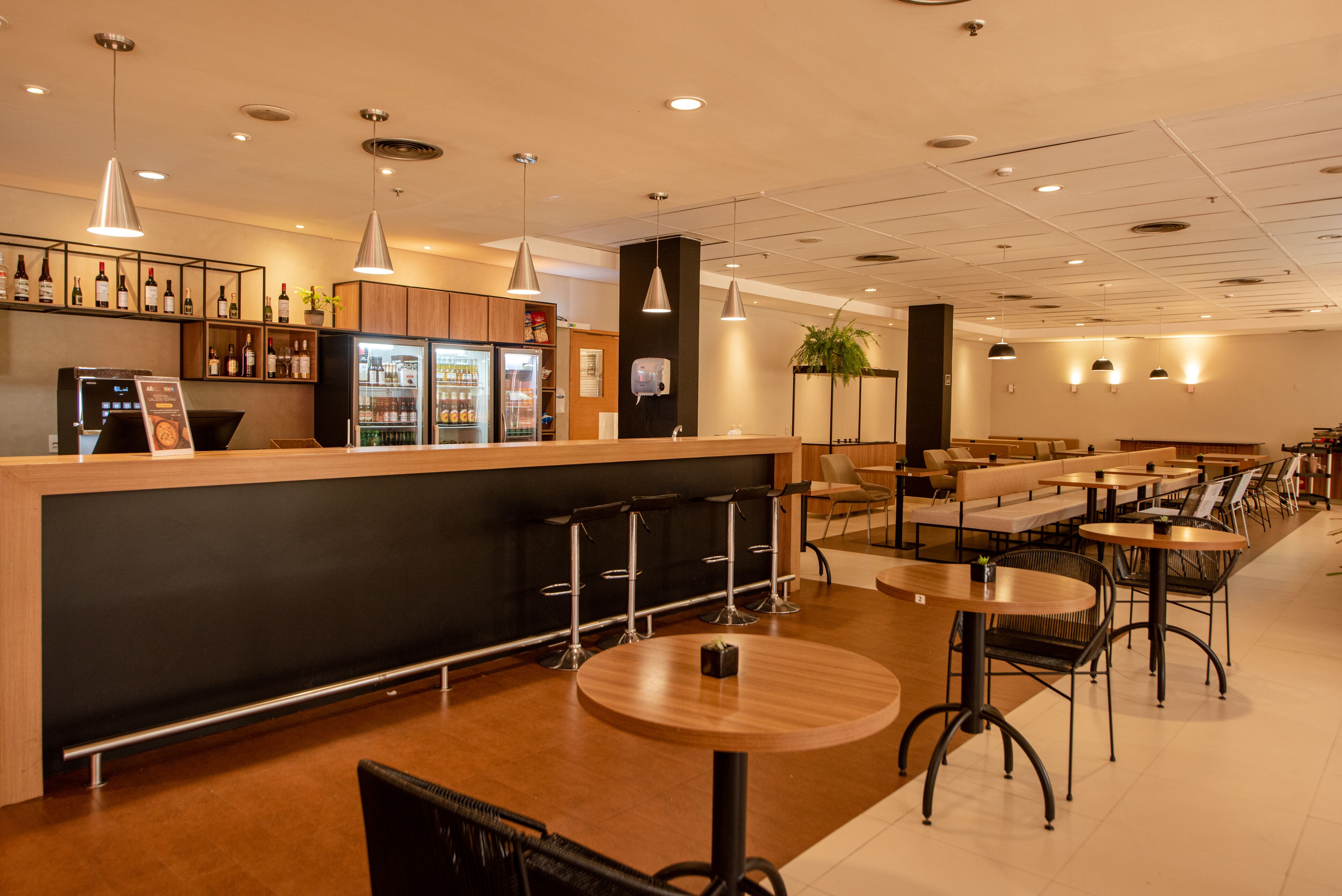 Um café moderno com área de bar, assentos e um refrigerador cheio de bebidas.