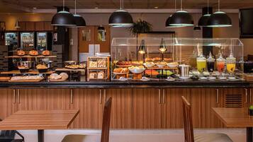 Um buffet de café da manhã com diversas opções de alimentos e bebidas, móveis de madeira e luminárias pendentes.