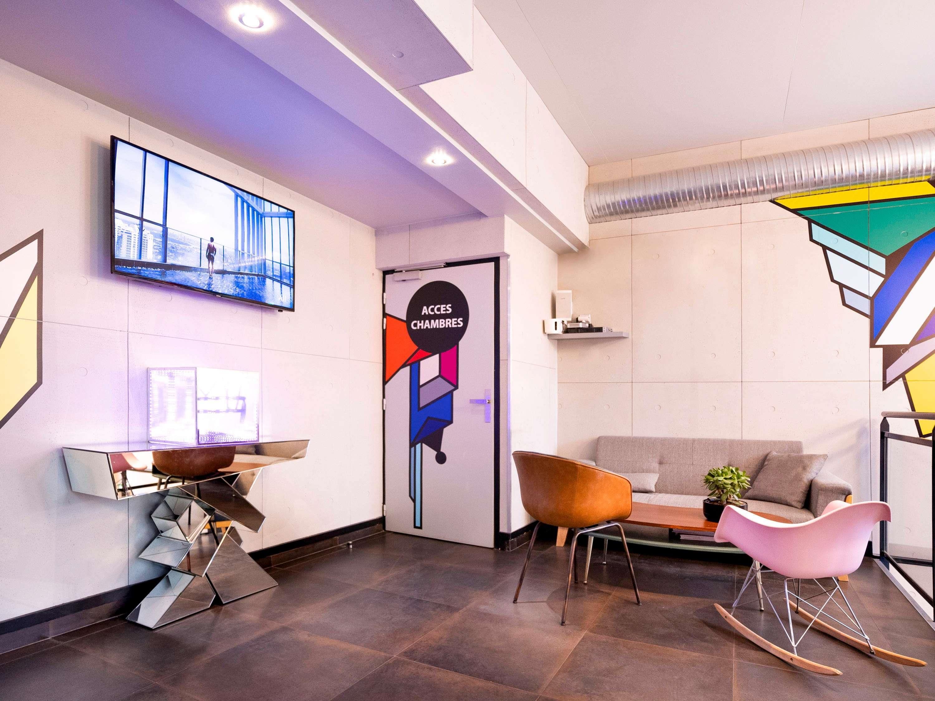Um lobby moderno com televisão de tela plana, um sofá, uma mesa de centro e uma peça de arte geométrica única na parede.