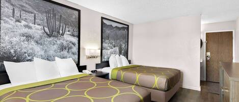 Quarto de hotel com duas camas, uma mesa de cabeceira, uma luminária e duas imagens emolduradas na parede.
