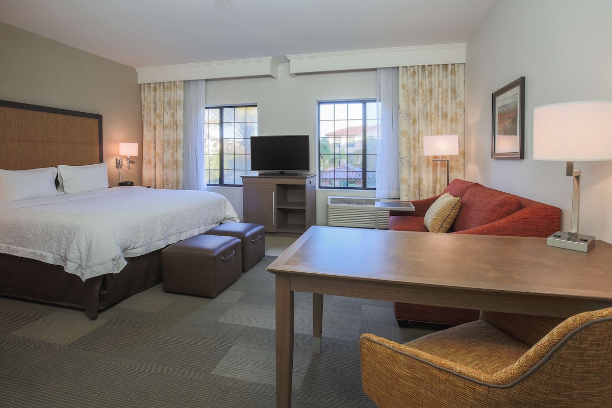 Quarto de hotel com cama, televisão, mesa, sofá vermelho e cadeira.