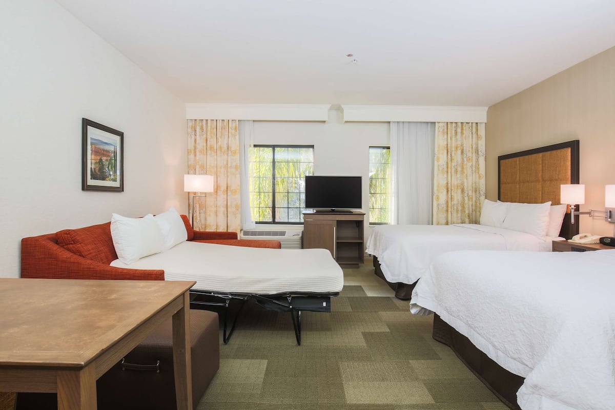 Quarto de hotel com duas camas, uma escrivaninha, televisão e um sofá.