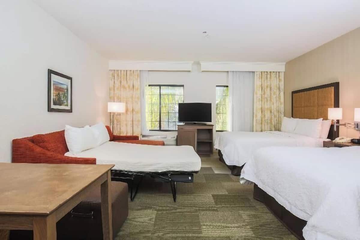 Quarto de hotel com duas camas, televisão, escrivaninha e uma cadeira.