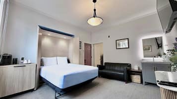 Quarto de hotel com cama, escrivaninha, cadeira, sofá, banheiro e luminária no teto.