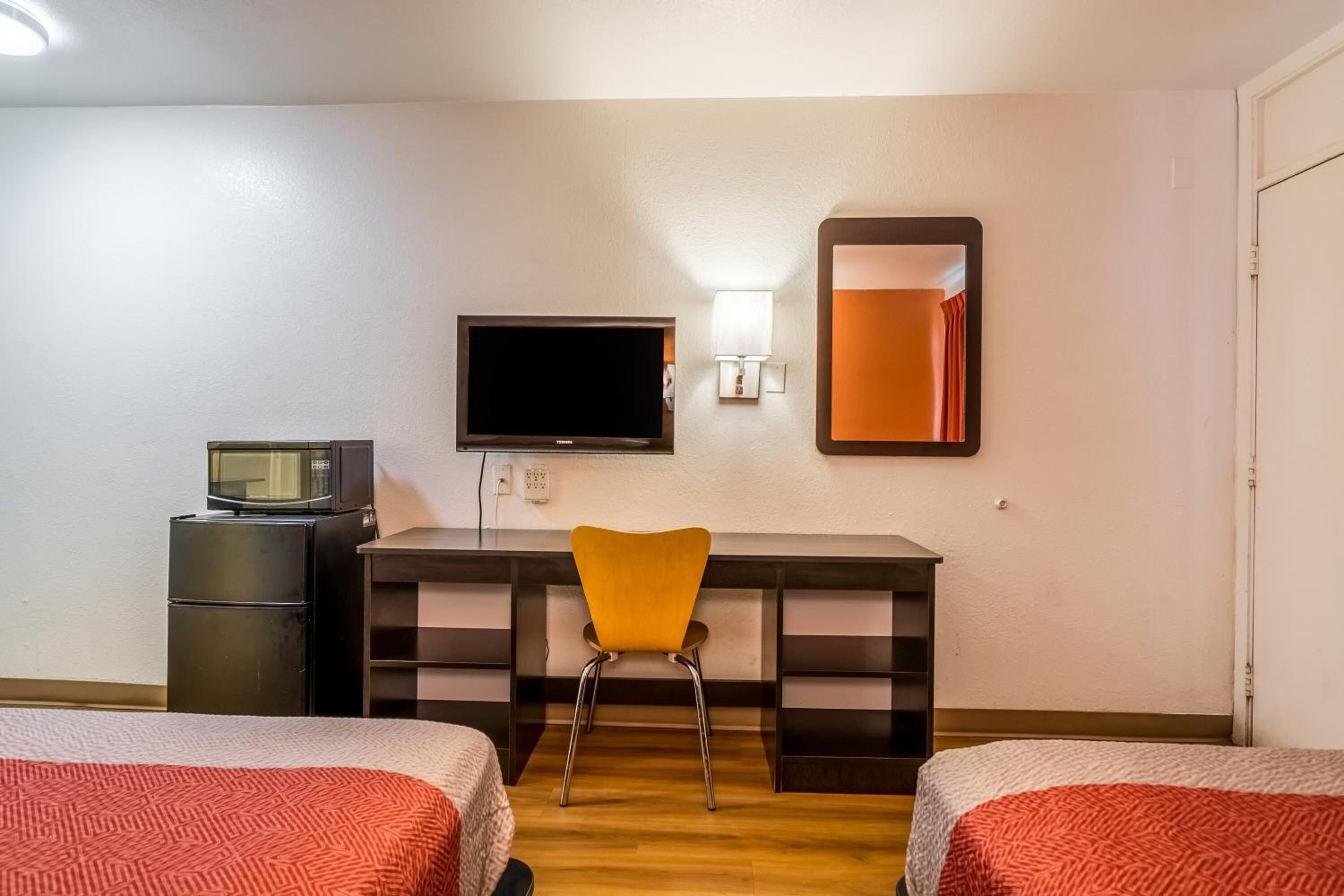 Quarto de hotel com duas camas, uma escrivaninha com cadeira, televisão, micro-ondas e espelho.
