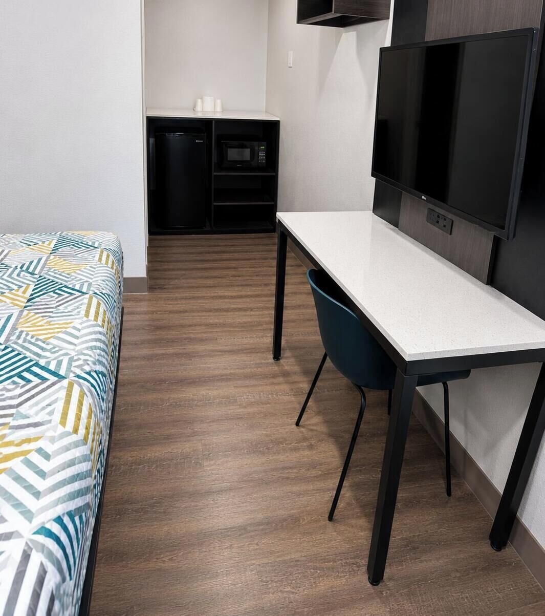 Quarto com cama, escrivaninha, cadeira, televisão e micro-ondas.