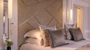 Quarto de hotel moderno com cabeceira estampada em padrão geométrico, mesa de cabeceira com um vaso de flores e uma cama bem arrumada com várias almofadas.