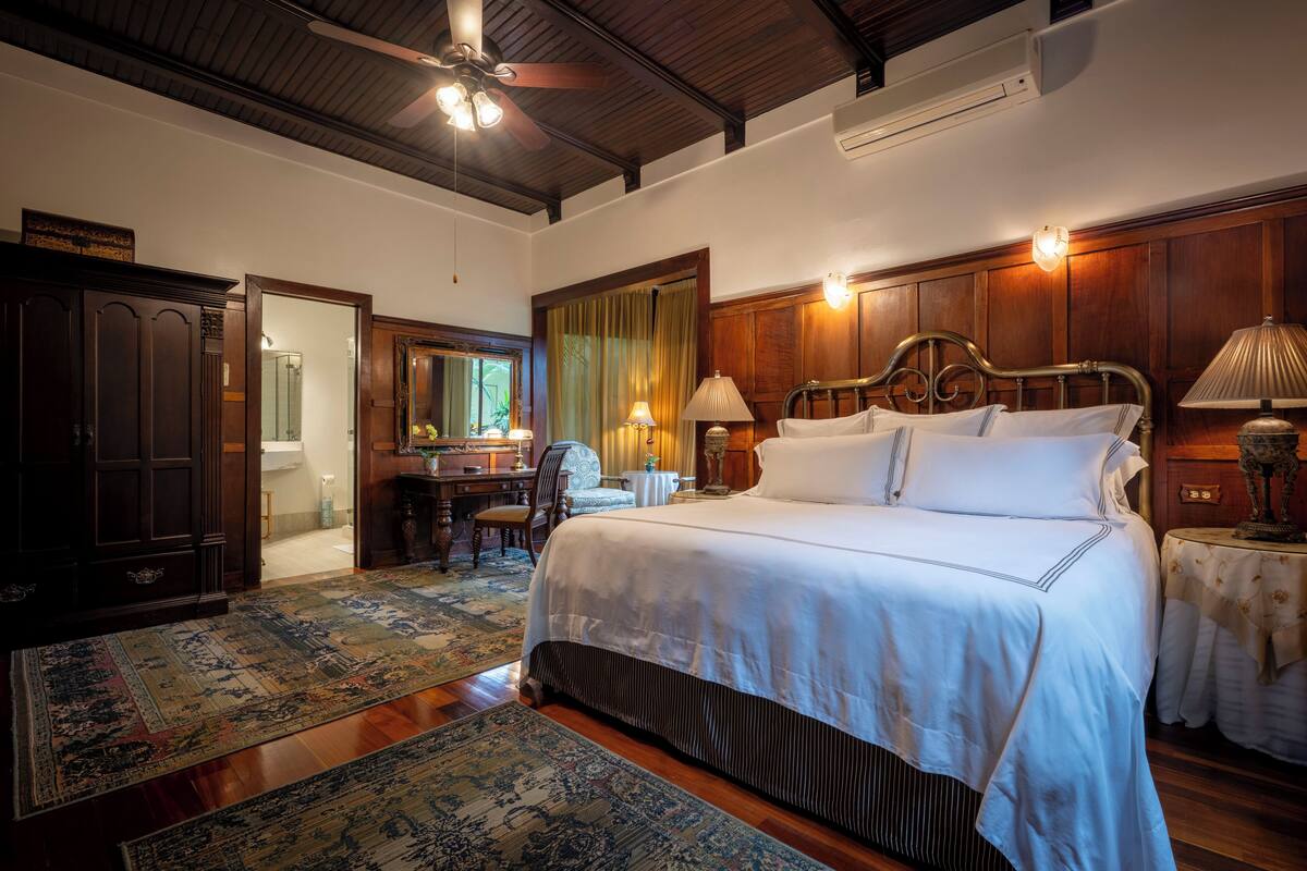 Um quarto espaçoso com uma cama grande, cabeceira de madeira e ventoinha no teto.