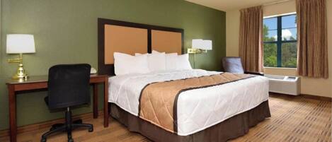 Quarto de hotel com cama, escrivaninha, cadeira e janela com cortinas.