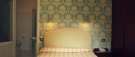 Quarto de hotel com cama, mesa de cabeceira e banheiro visível por uma porta aberta.