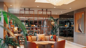 Um saguão moderno com área de estar central, um grande candelabro e vista para o bar.