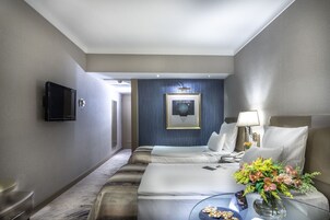 Quarto de hotel com duas camas, uma televisão de tela plana, uma obra de arte emoldurada, um abajur, um vaso com flores e uma pequena mesa com um telefone e um bloco de notas.