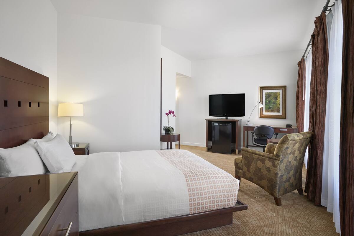 Quarto de hotel com uma cama grande, uma mesa com computador, televisão e uma cadeira.