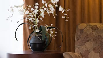 Uma orquídea em vaso sobre uma mesa de madeira redonda, com um sofá estampado ao fundo.