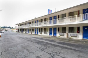 Um motel com estrutura de dois andares, vários quartos com portas azuis e uma varanda no andar superior.