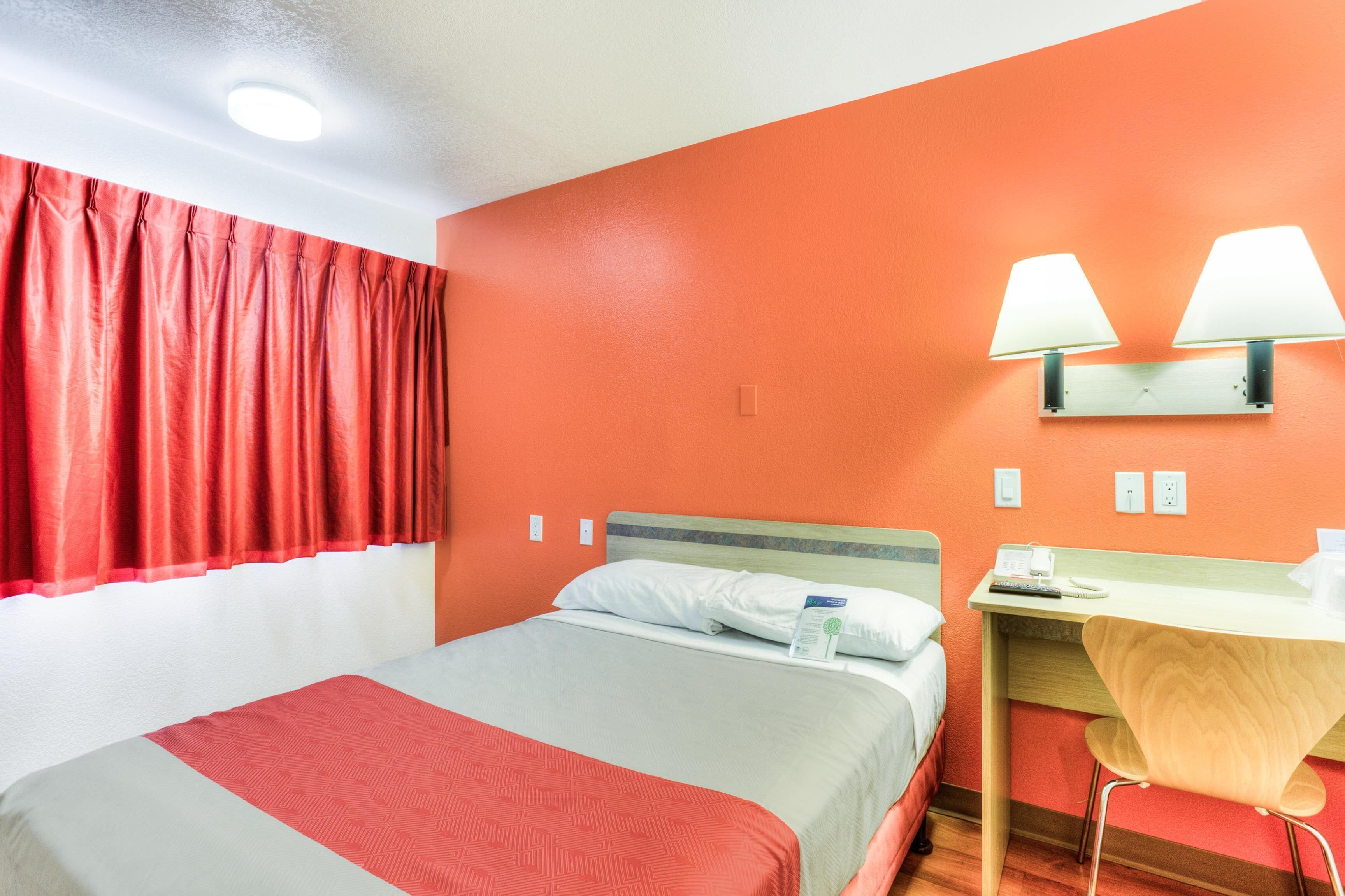 Quarto de hotel com uma cama, uma secretária e duas luminárias fixadas na parede.