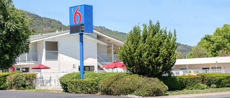 Um motel com um letreiro grande com o número '6', uma área de estar coberta ao ar livre e vista para colinas ao fundo.