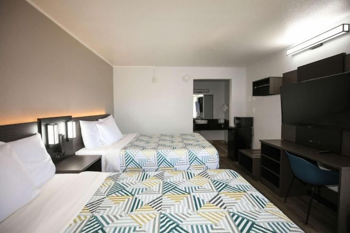 Quarto de hotel com duas camas, uma escrivaninha, uma cadeira, uma televisão e um espelho.