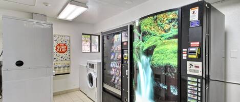 Uma lavanderia com máquina de lavar, secadora e máquina de vendas com painel em cascata.